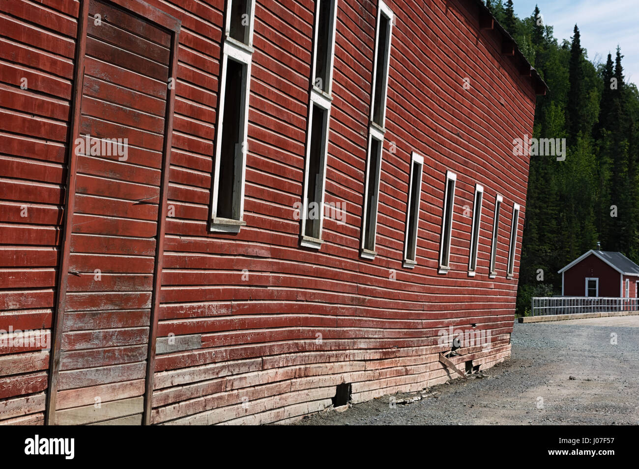 Empty windows form a curvy line along a red plank building that is ...