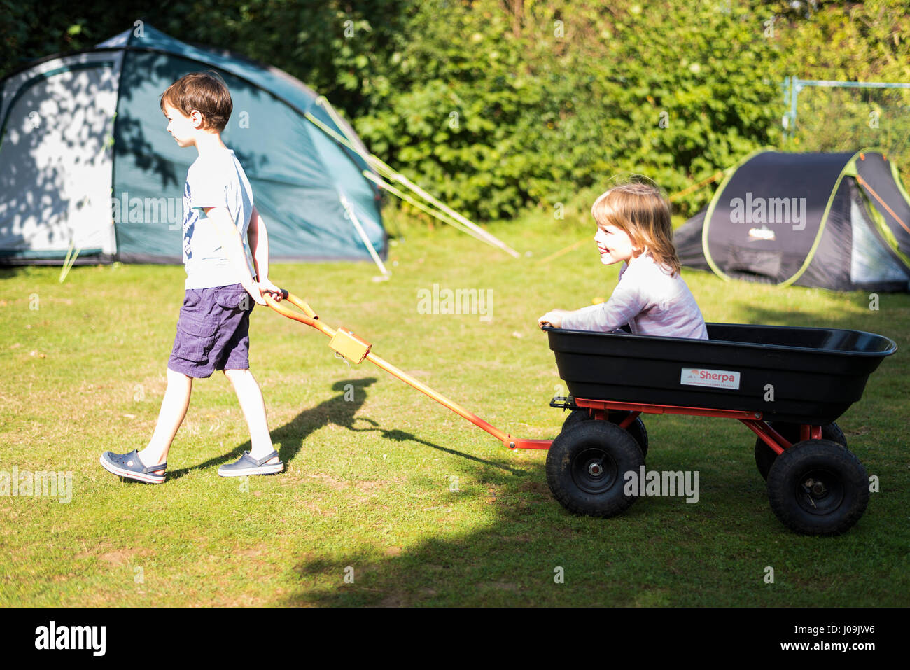 A child pulling his friend in a hand cart at a festival in the summer ...
