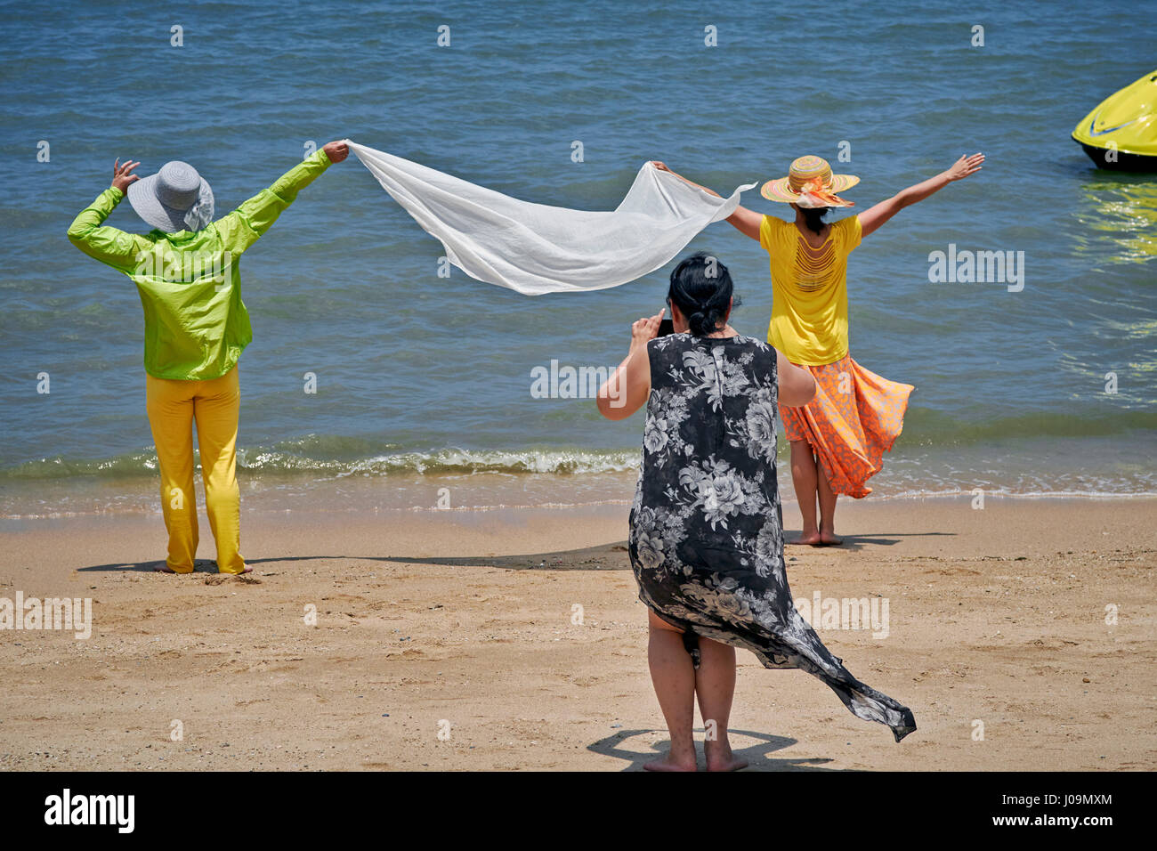 Woman taking photo of her female friends on the beach. Women colorful ...