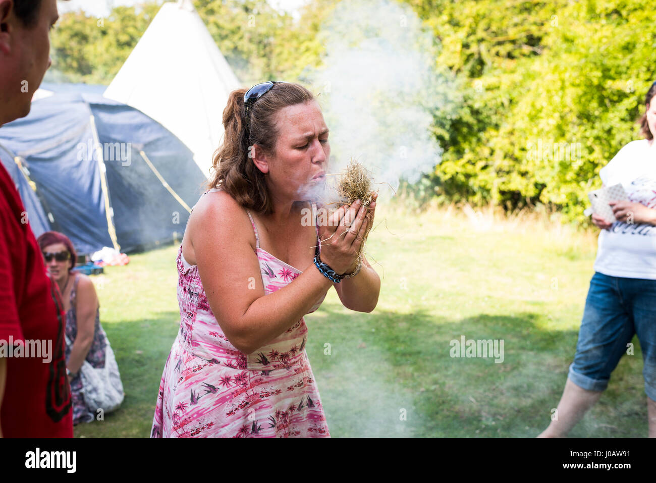 Woman blowing a small ember in a bundle of straw in a firelighting ...