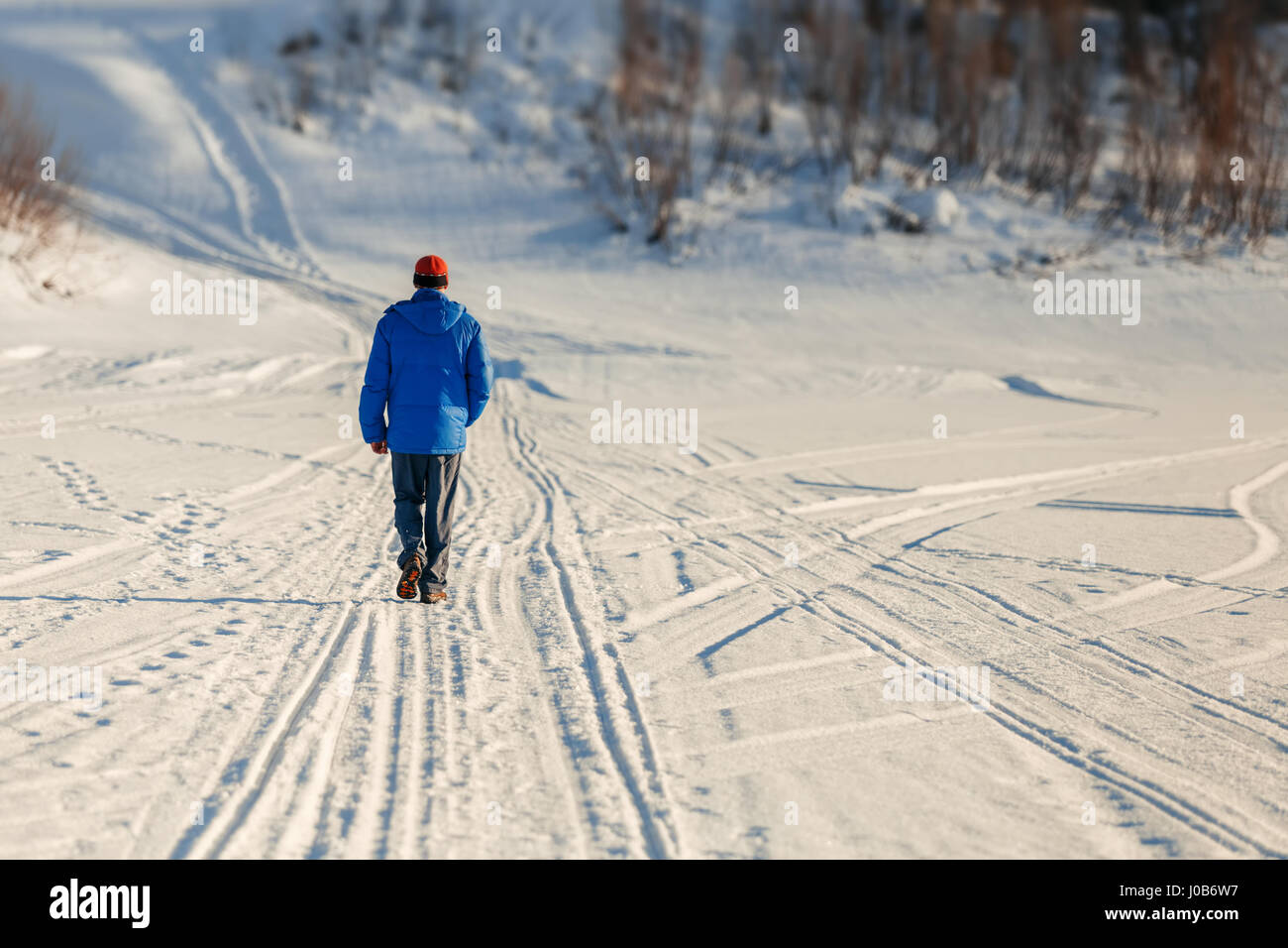 young man in a blue jacket crossing the river on the ice in winter ...