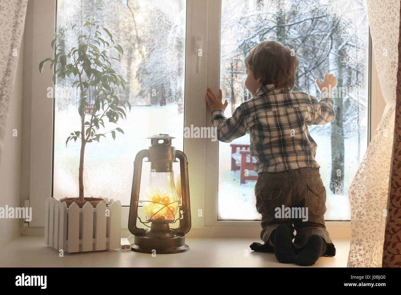 boy sitting on a white window sill and looks out the window Stock Photo ...