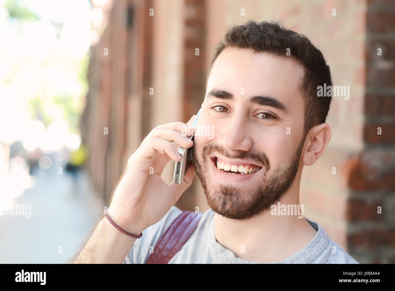 Portrait of young latin man talking on the phone against brick wall ...