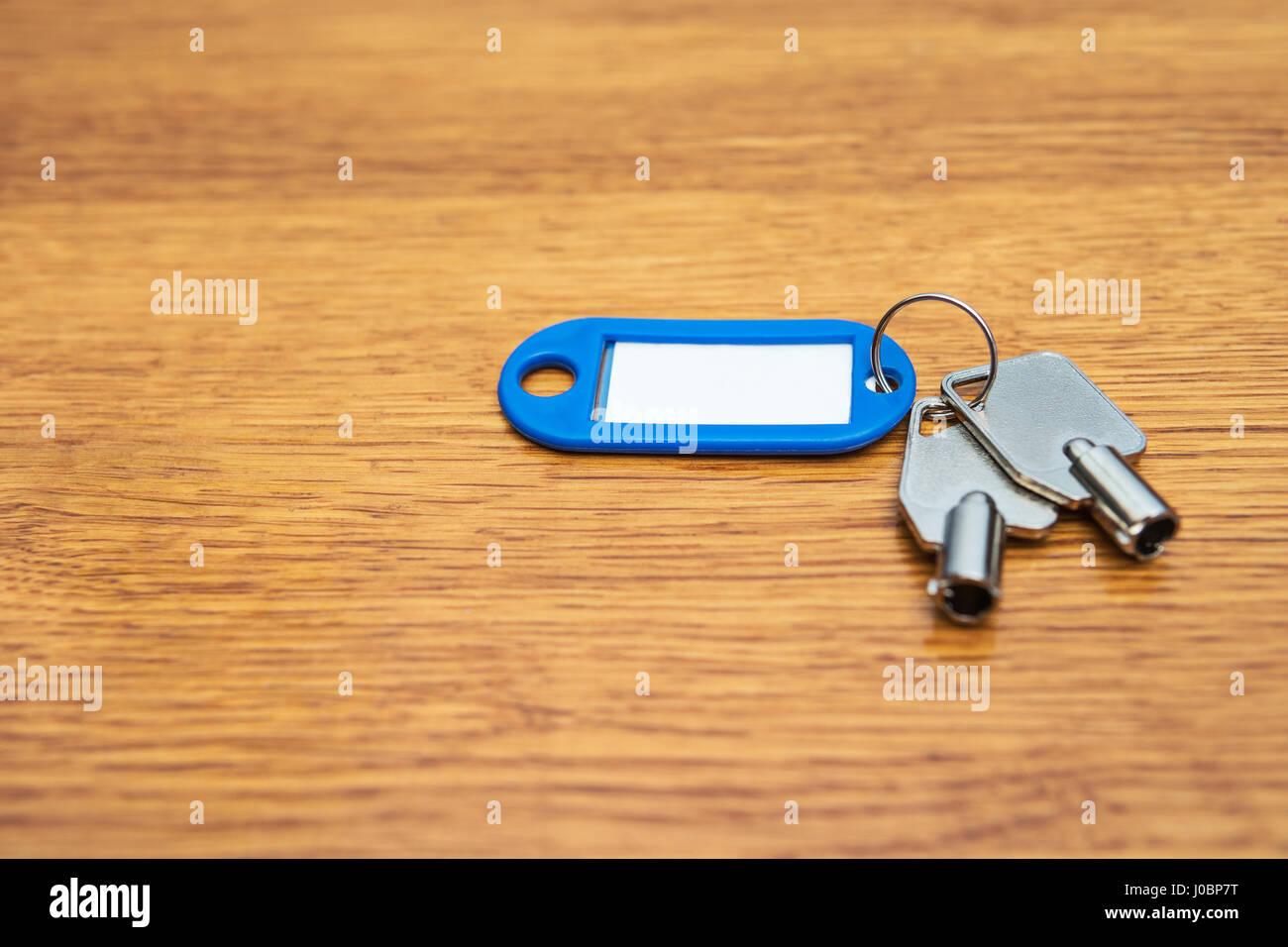 Two metal keys with a blue blank tag lying on a wooden table Stock ...
