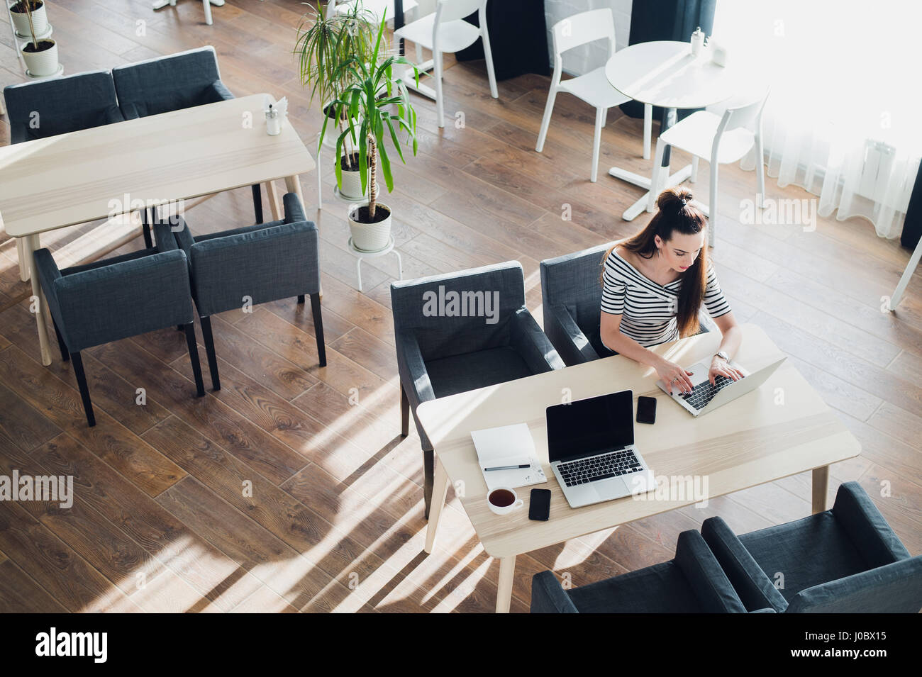 Overhead view of businesswoman at table of staff canteen, typing on a ...