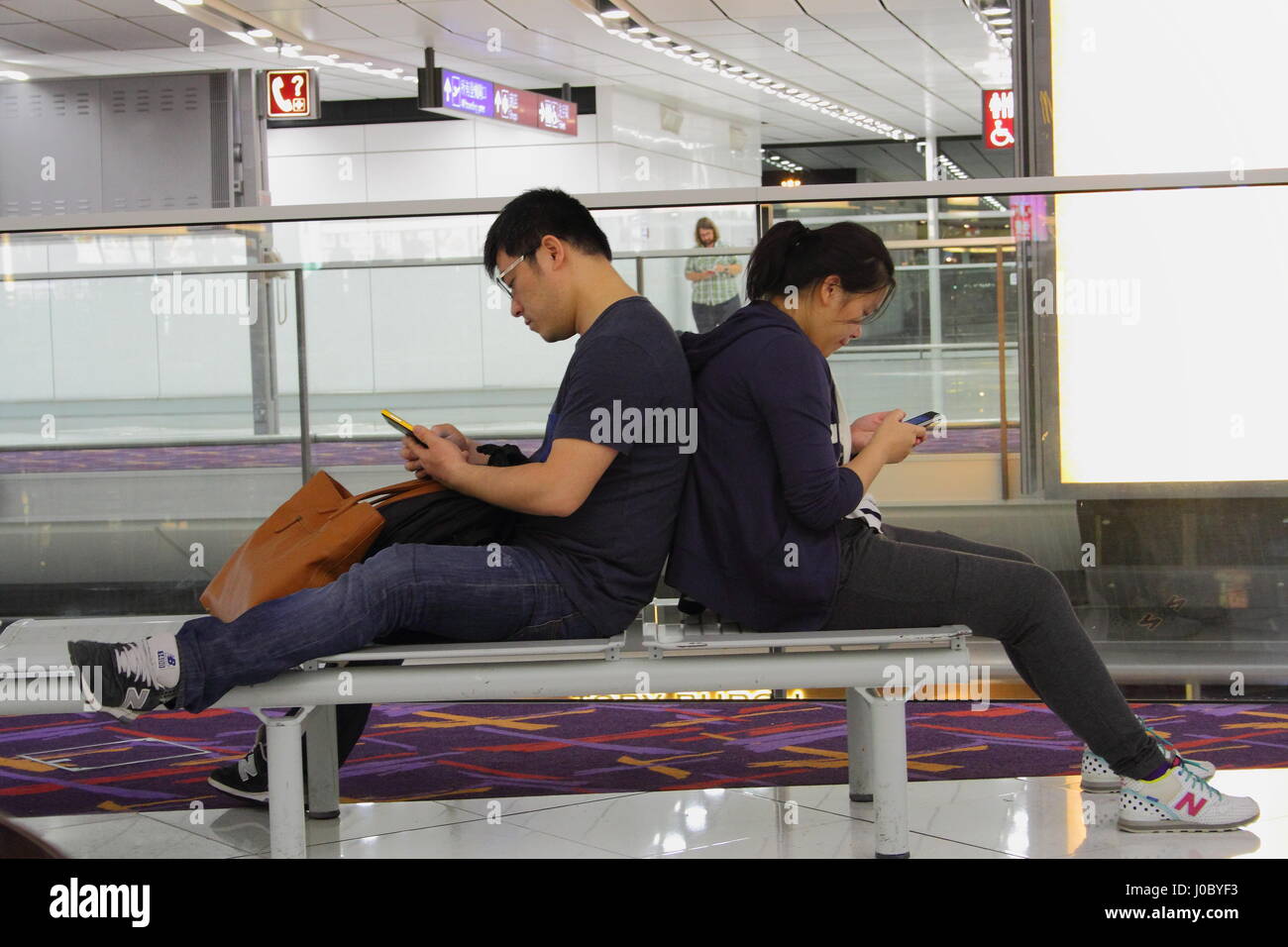 The smart phone generation - a young couple sitting back-to-back busy ...