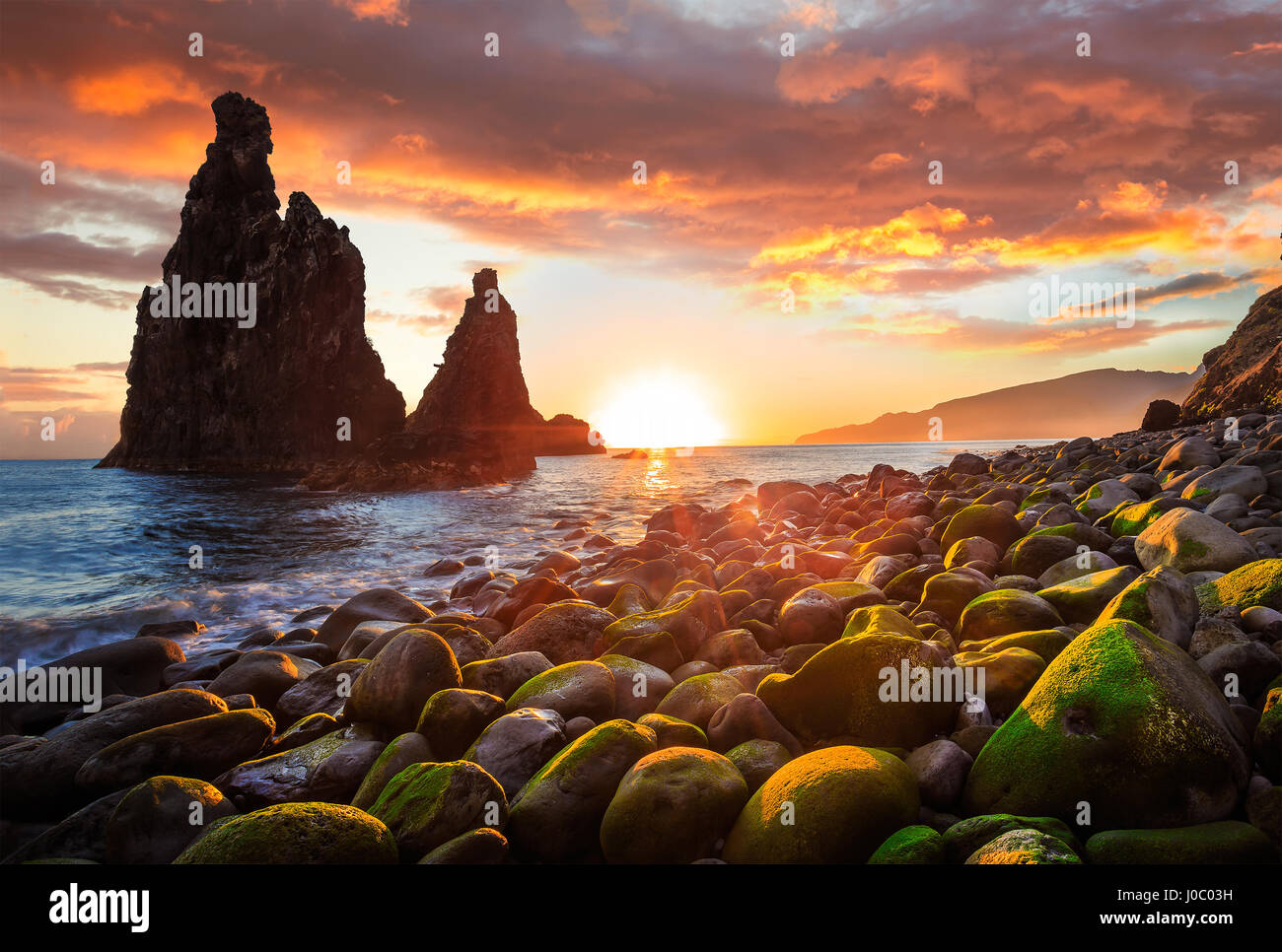 Colorful sunrise at Ribeira da Janela beach, with moss covered rocks ...