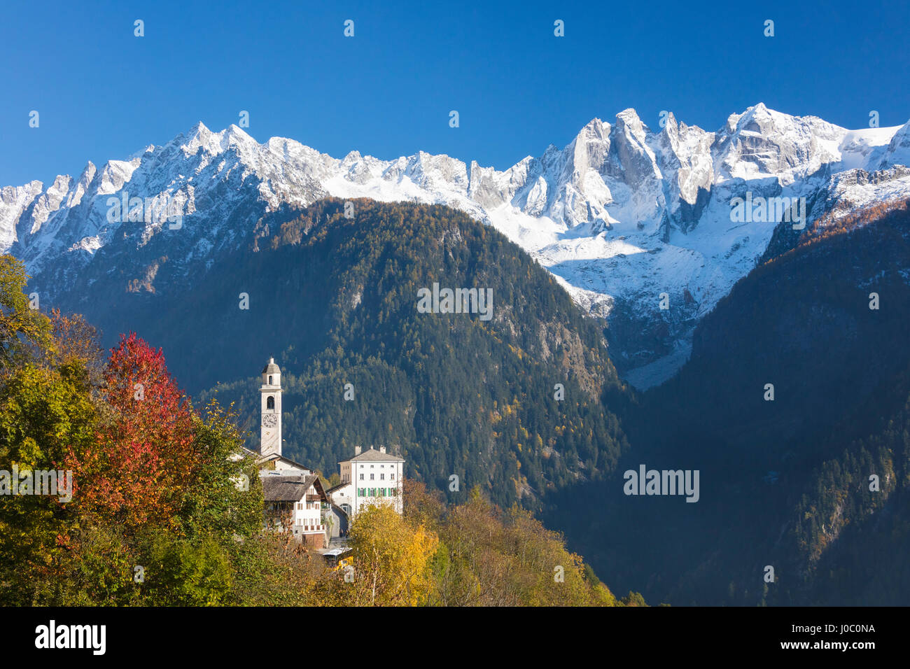 The colorful trees frame the alpine church and the snowy peaks, Soglio ...