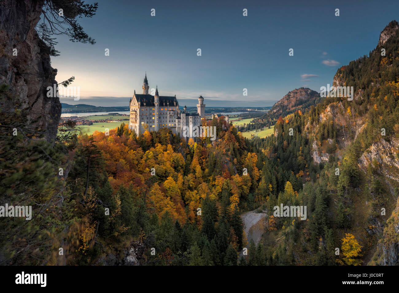 Dusk lights on Neuschwanstein Castle surrounded by colorful woods in ...