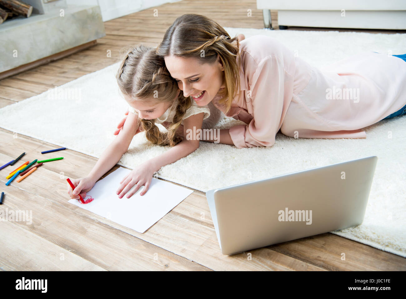 side view of smiling mother looking how concentrated daughter drawing ...