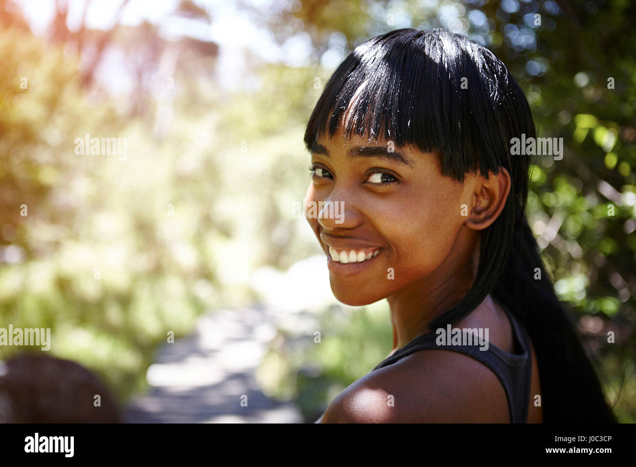 Portrait of young woman, outdoors, looking over shoulder, smiling Stock ...