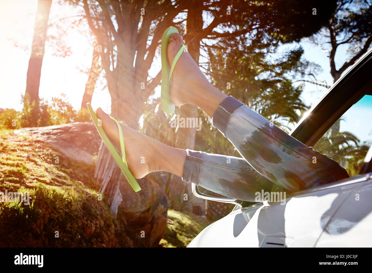 Young woman lying in car, legs dangling out of car window Stock Photo ...