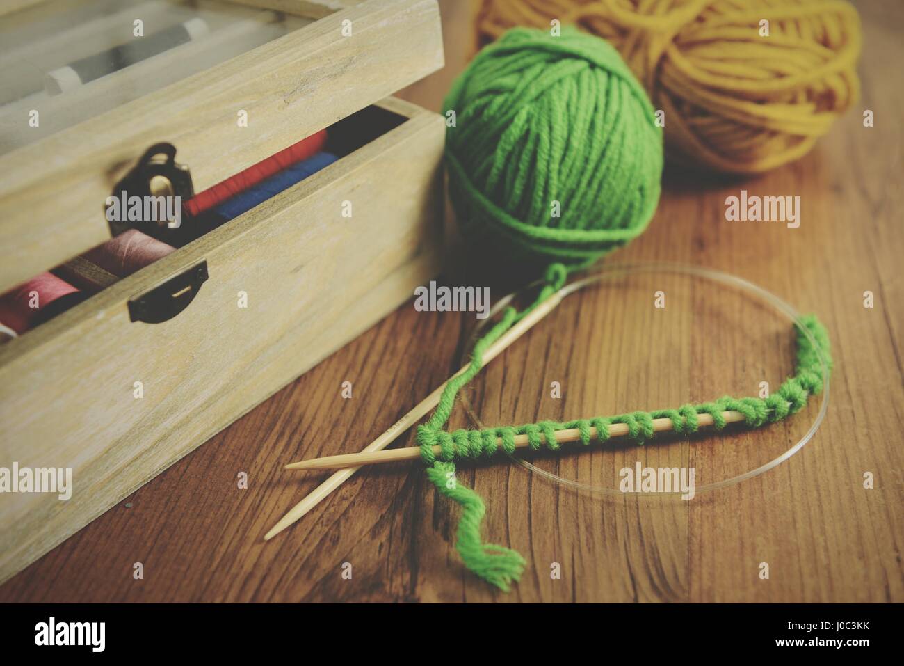 knitting with green wool on wooden table and balls in a sew box ...