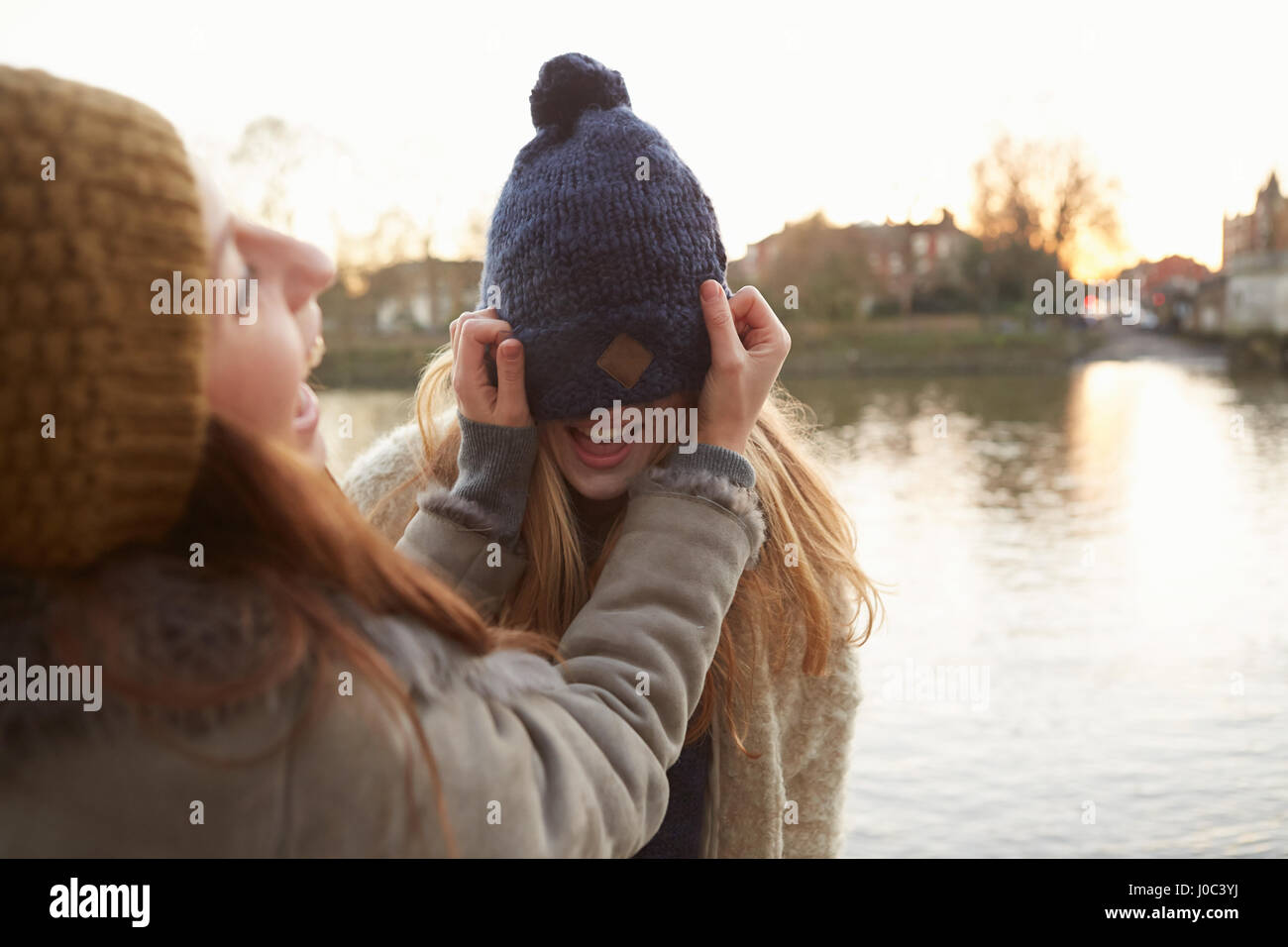 Young woman putting knitted hat on friend, hat covering eyes, laughing ...