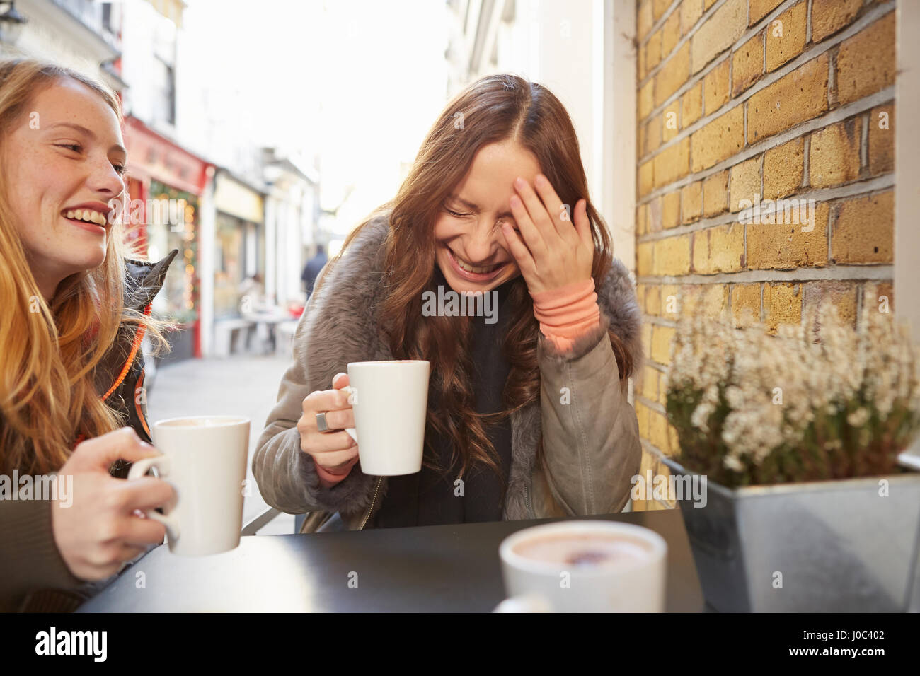 Two female friends, sitting outdoors, drinking coffee, laughing Stock ...