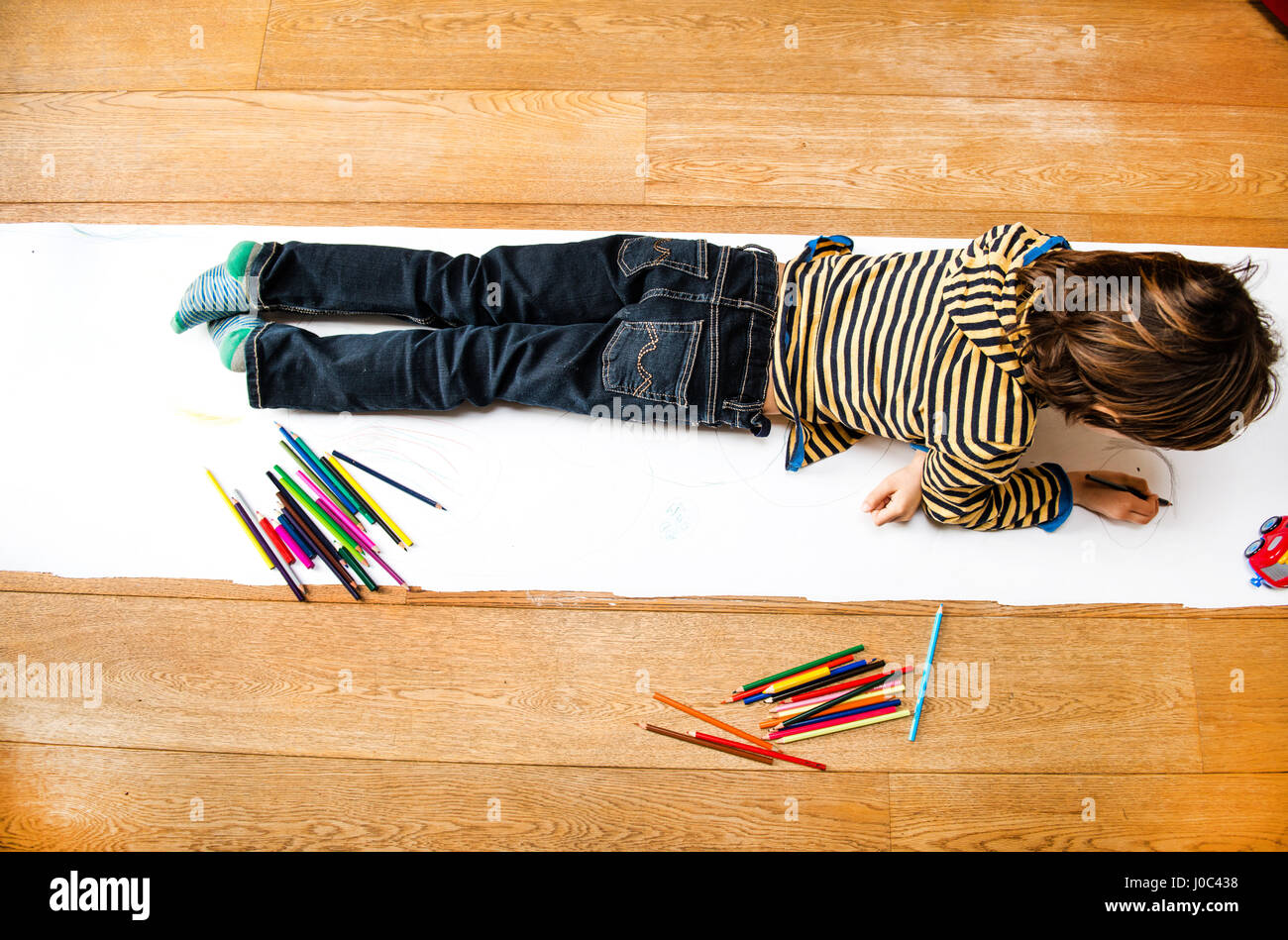 Overhead view of boy lying on top of and drawing on long paper Stock ...