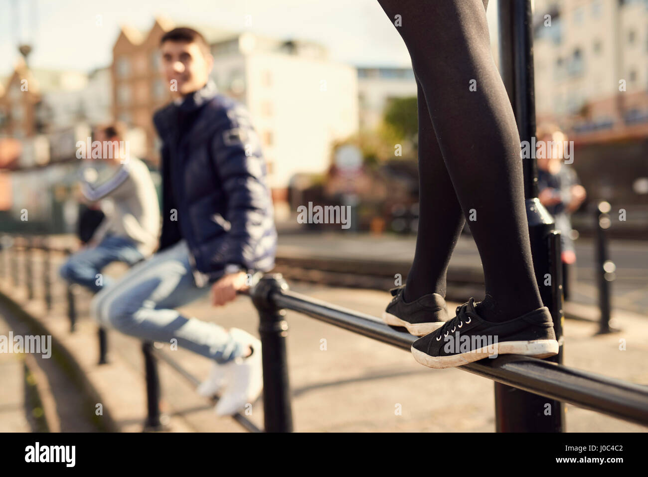 Young man sitting on railing, young girl walking along railing next to ...