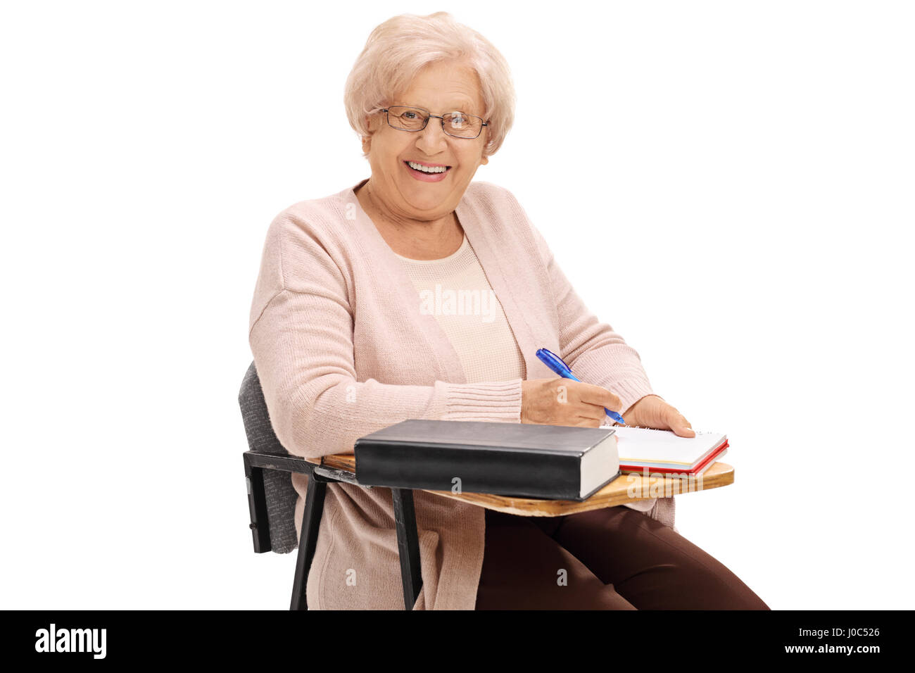 Elderly student in a school chair taking notes and looking at the ...
