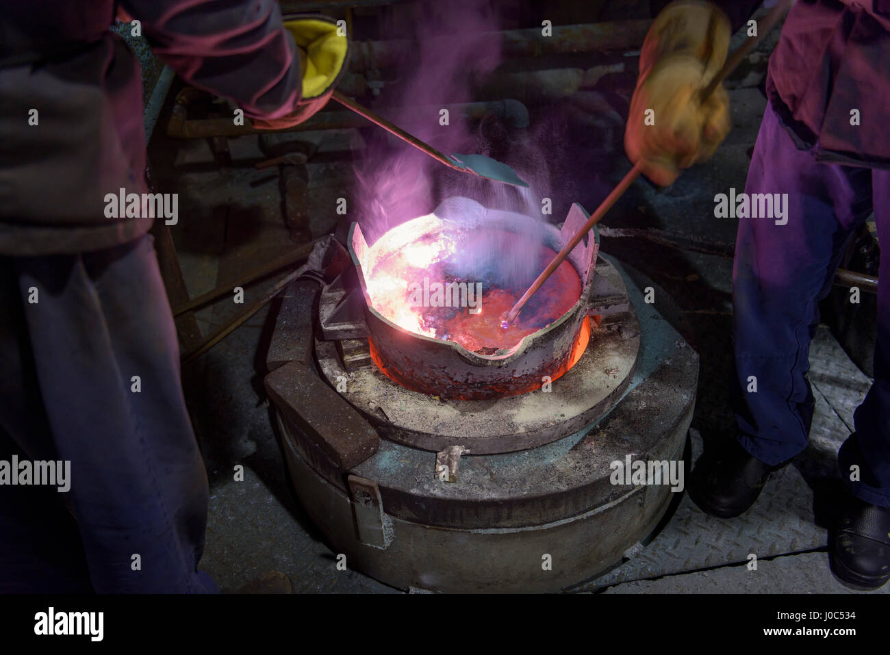 Workers stirring molten aluminium alloy in precision casting factory ...