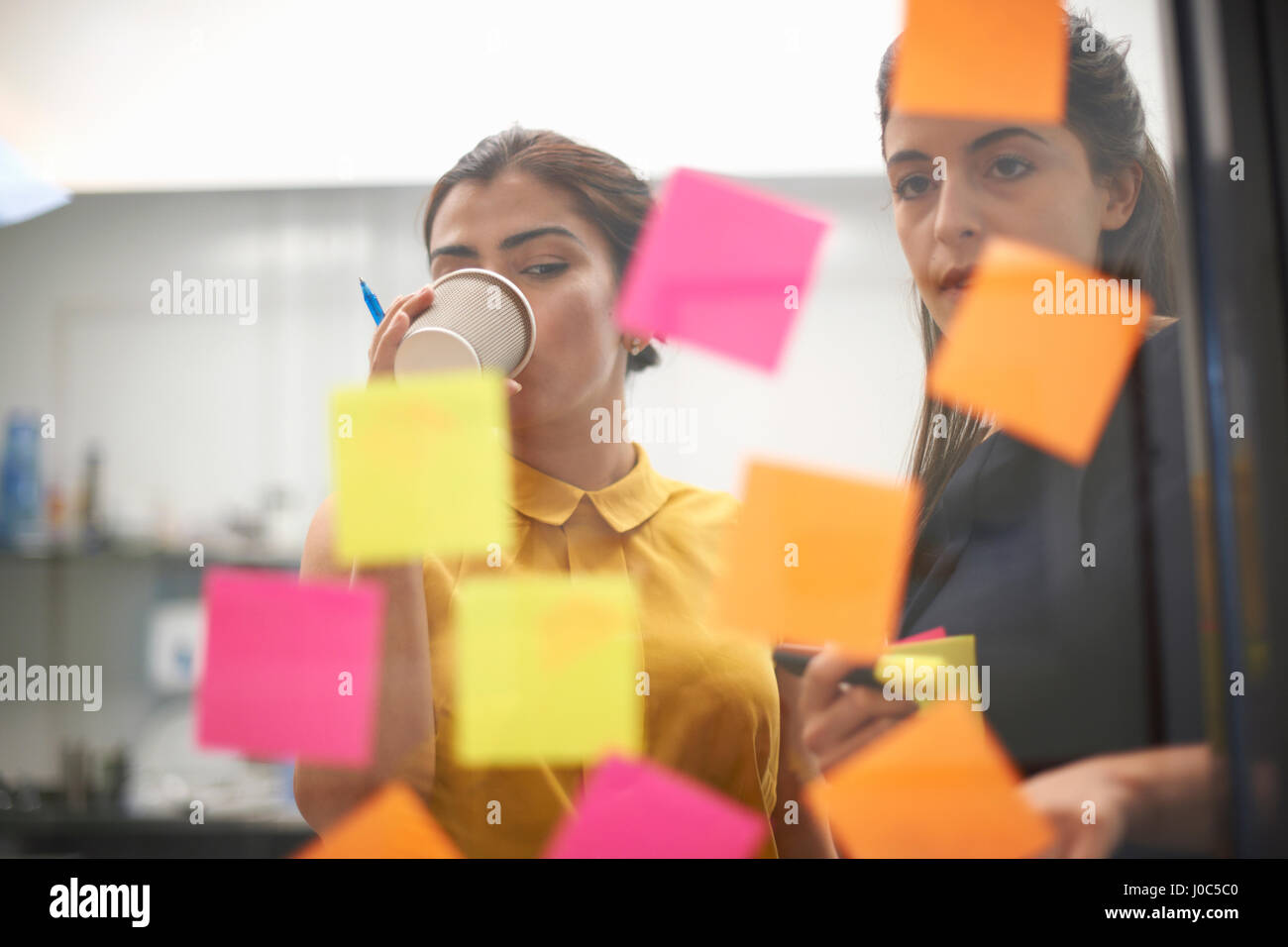 Two businesswomen drinking coffee and staring at sticky notes on office ...