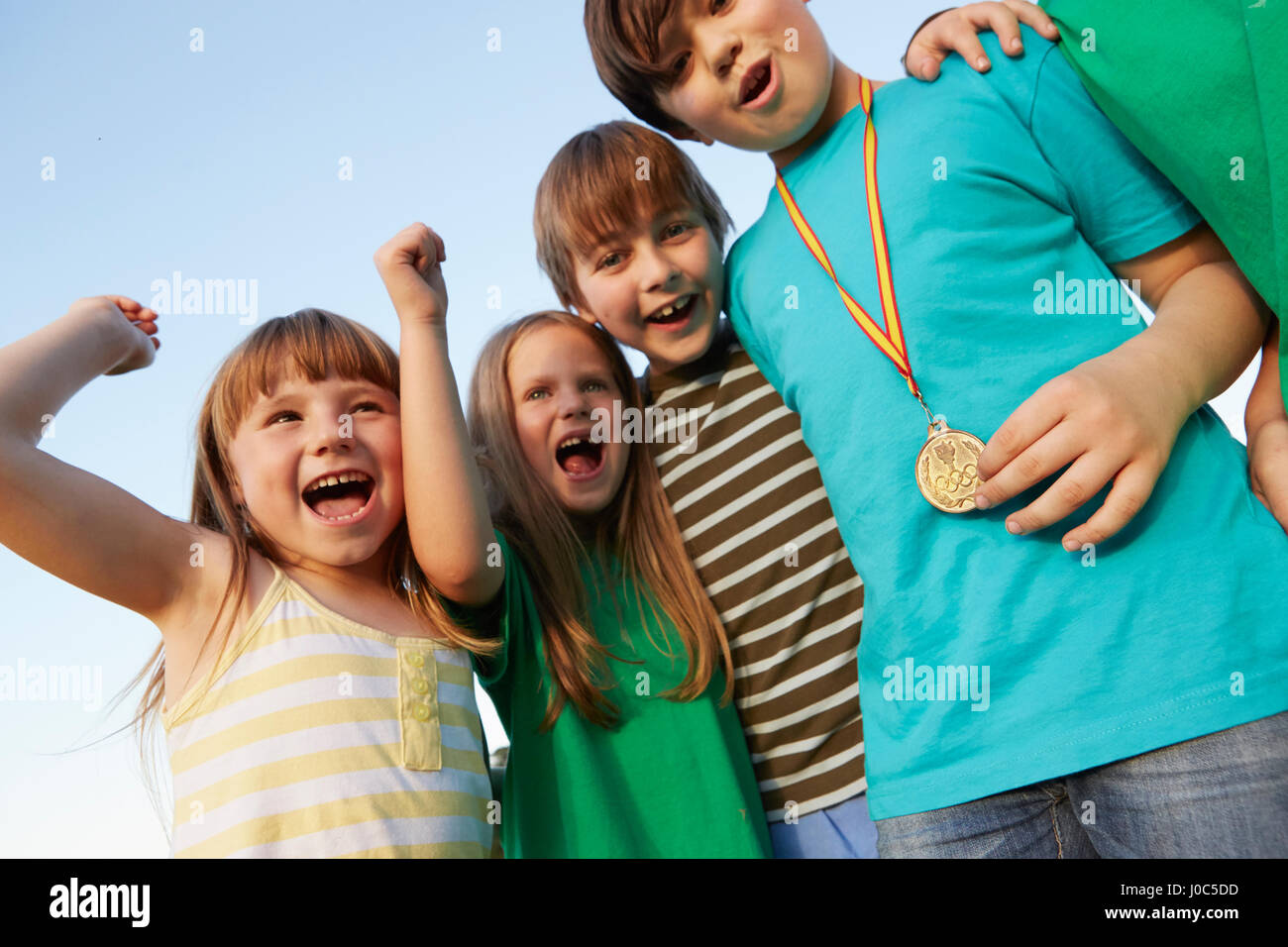Boy with gold medal and team cheering against blue sky Stock Photo - Alamy