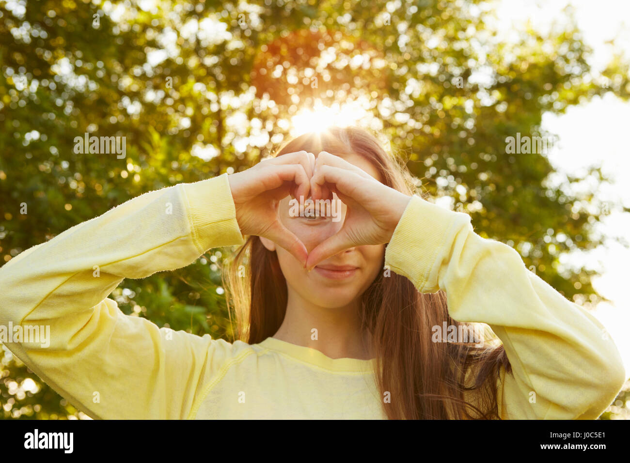 Portrait of girl making heart shape with hands in park Stock Photo - Alamy