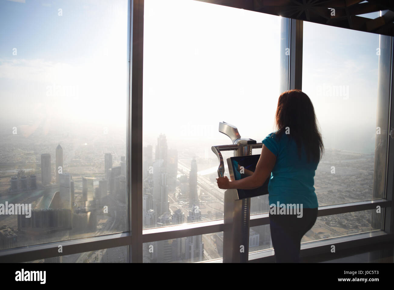 Rear view of female tourist looking through skyscraper window above the ...