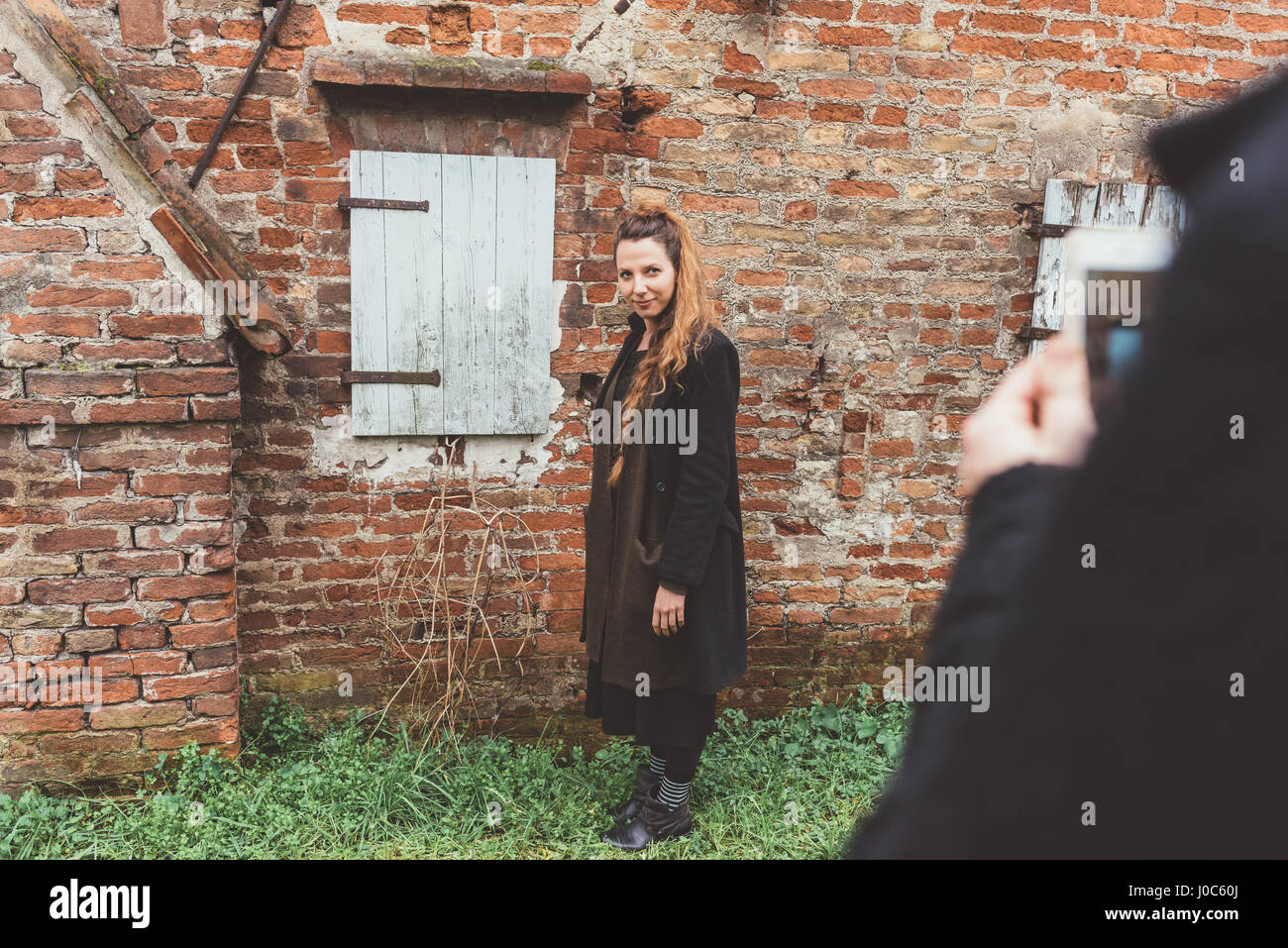 Over shoulder view of man photographing girlfriend by old brick wall ...