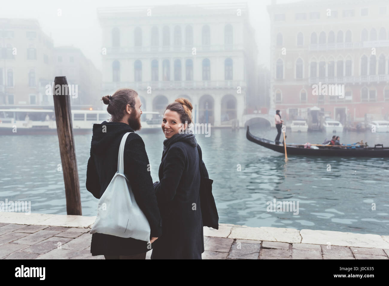 Rear view of couple on misty canal waterfront, Venice, Italy Stock ...