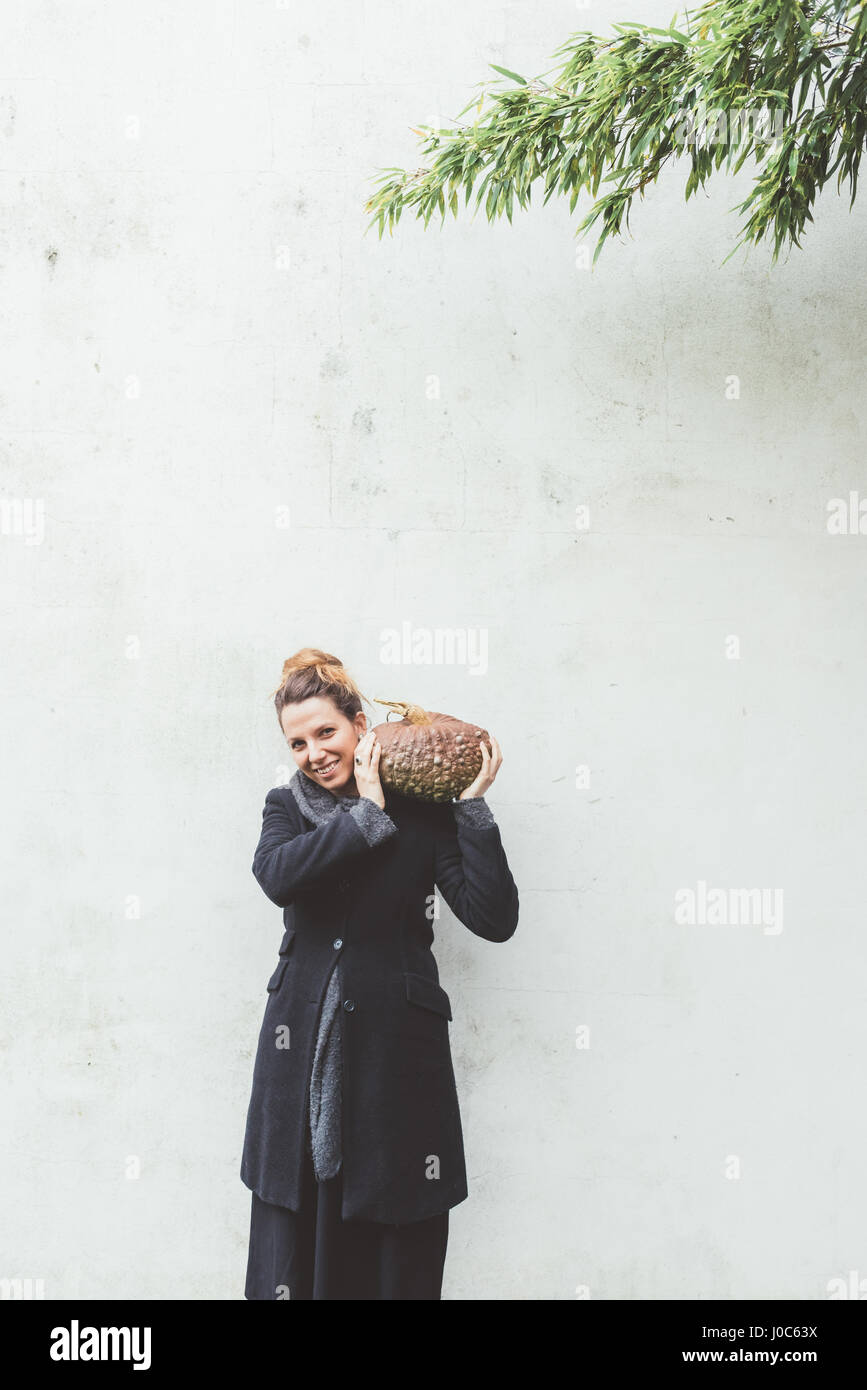 Portrait of young woman carrying pumpkin on shoulder in front of white ...