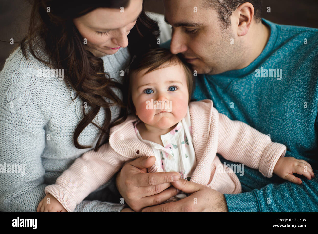 Baby girl looking up while being snuggled by her parents Stock Photo ...