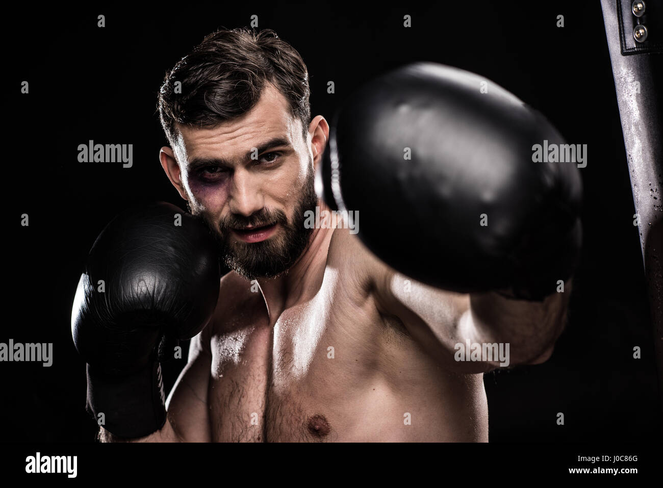 Young professional boxer with black eye punching and looking at camera ...