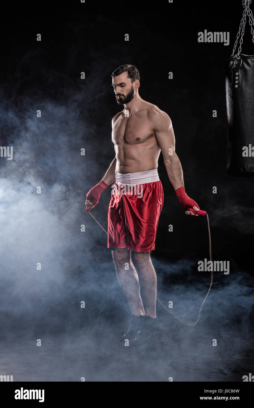 Young professional boxer with wrapped hands skipping on black Stock ...