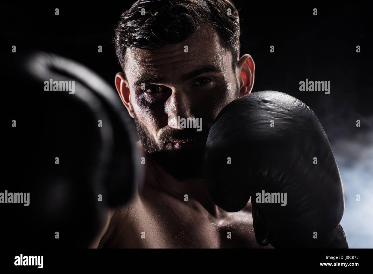 Young black eyed boxer in gloves punching and looking at camera Stock ...