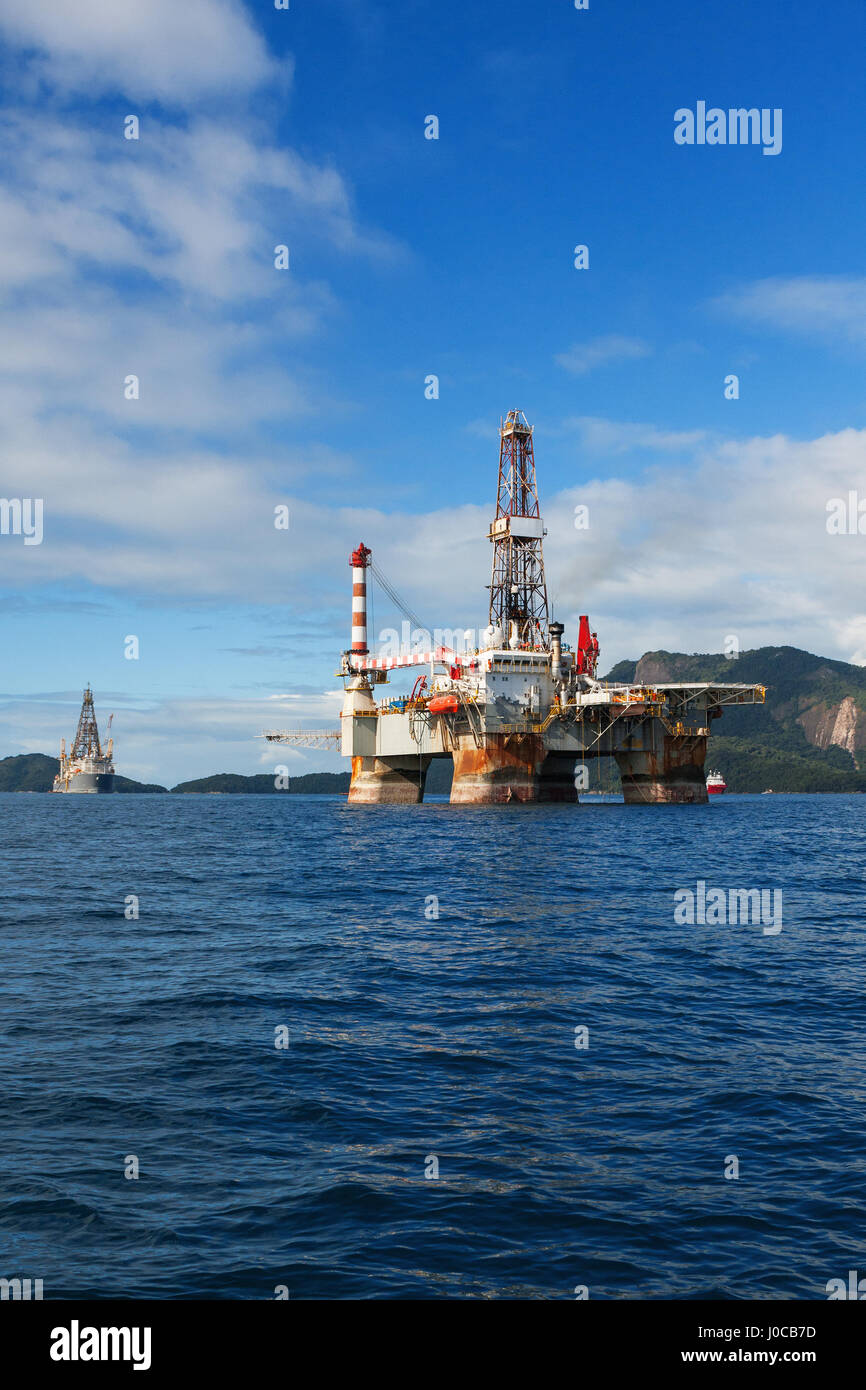 Offshore oil rig in front of green mountains with a blue sky above. A ...