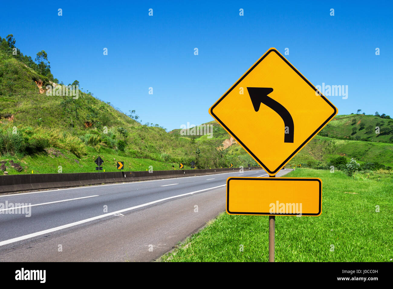 Yellow turn left road sign with empty road Stock Photo - Alamy