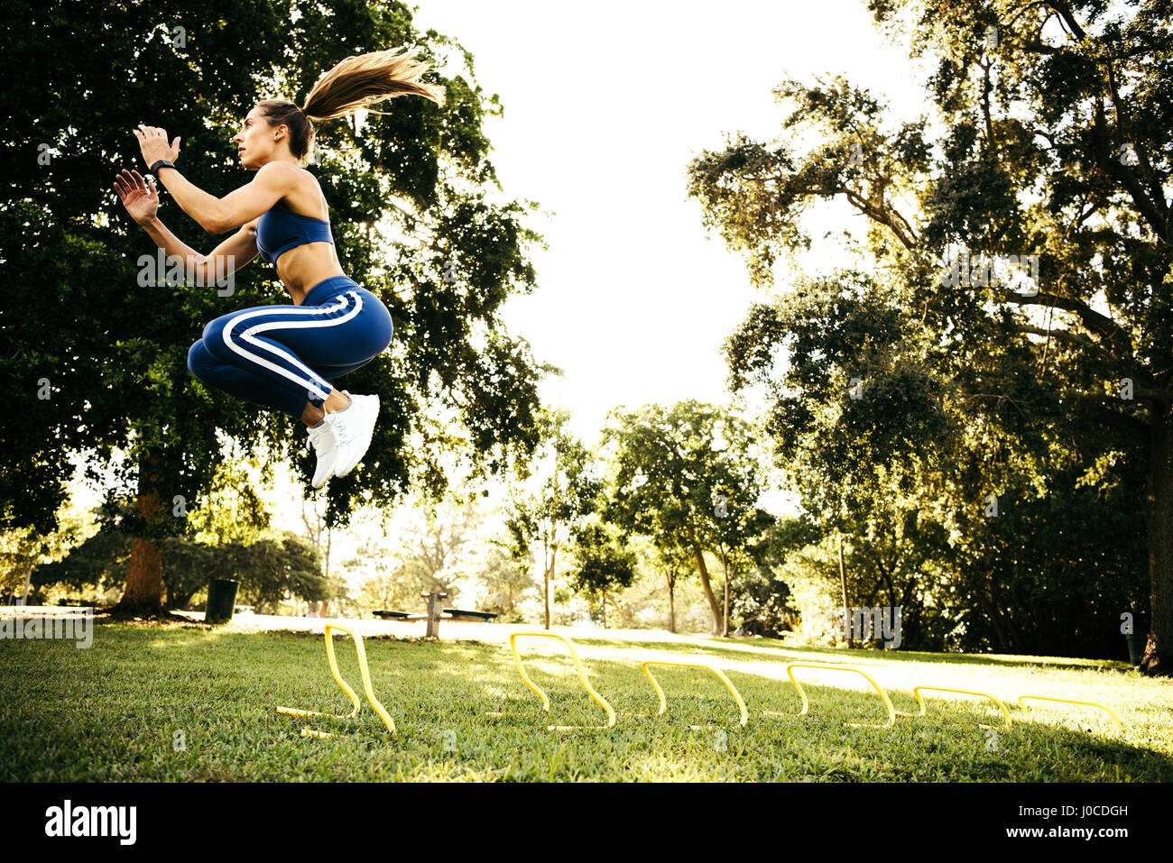 Young woman training, jumping between agility hurdles in park Stock ...