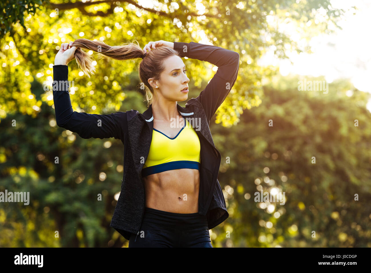 Young female runner tying up pony tail in park Stock Photo - Alamy