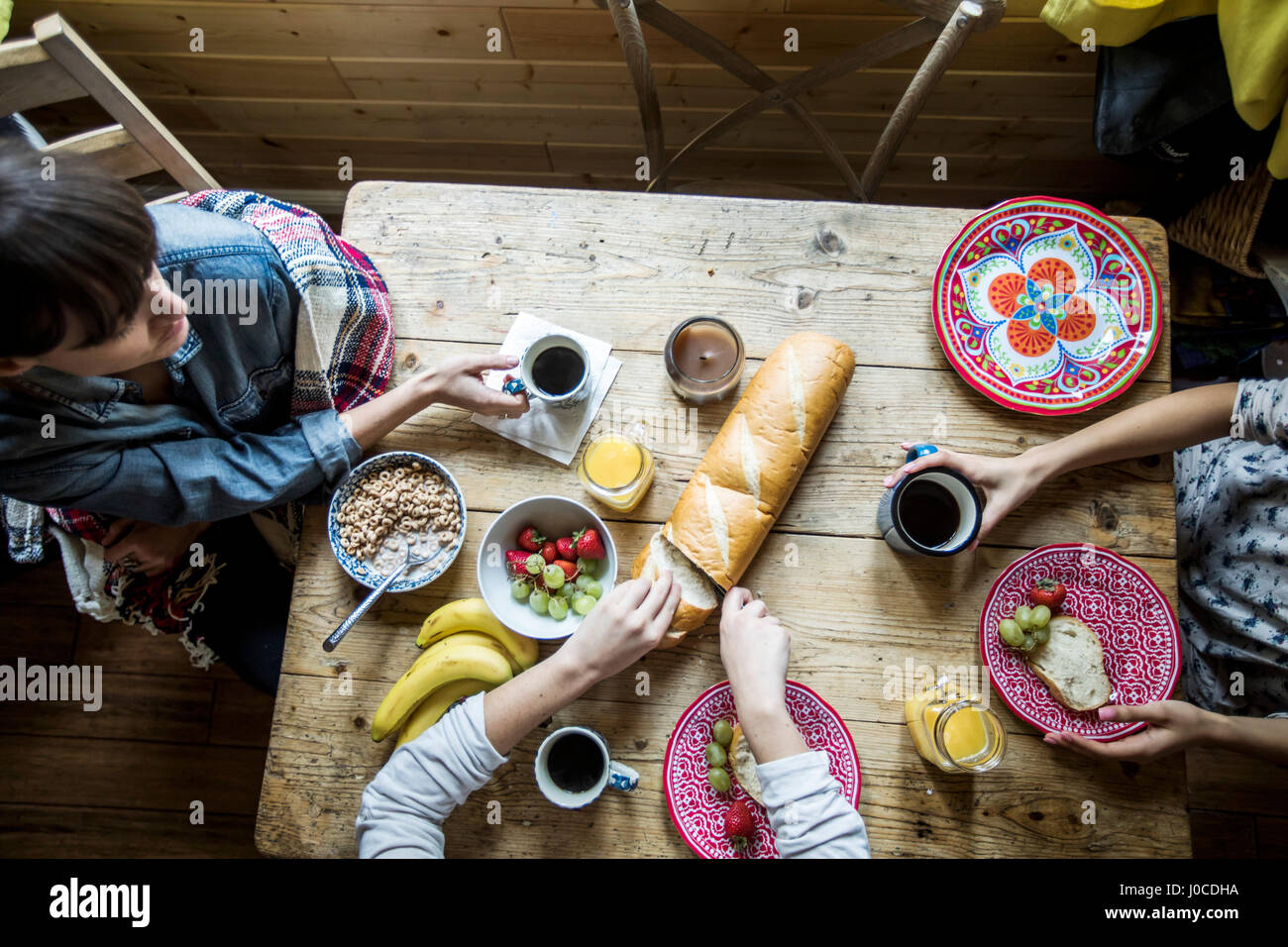 Three friends sitting around table, eating breakfast Stock Photo - Alamy
