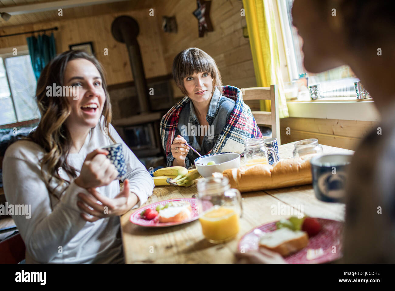 Three friends sitting around table, eating breakfast Stock Photo - Alamy