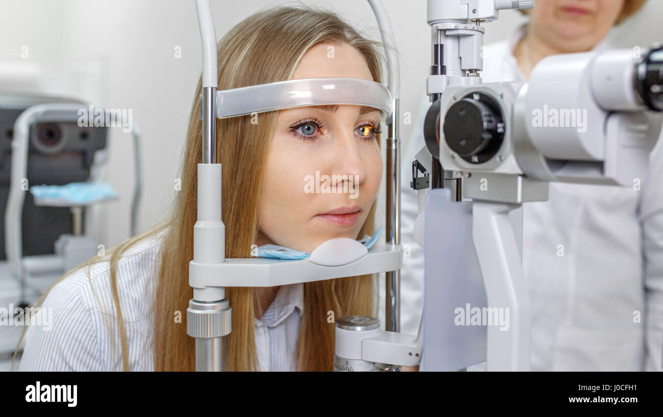 pretty young woman having her eyes examined by an eye doctor on a slit ...