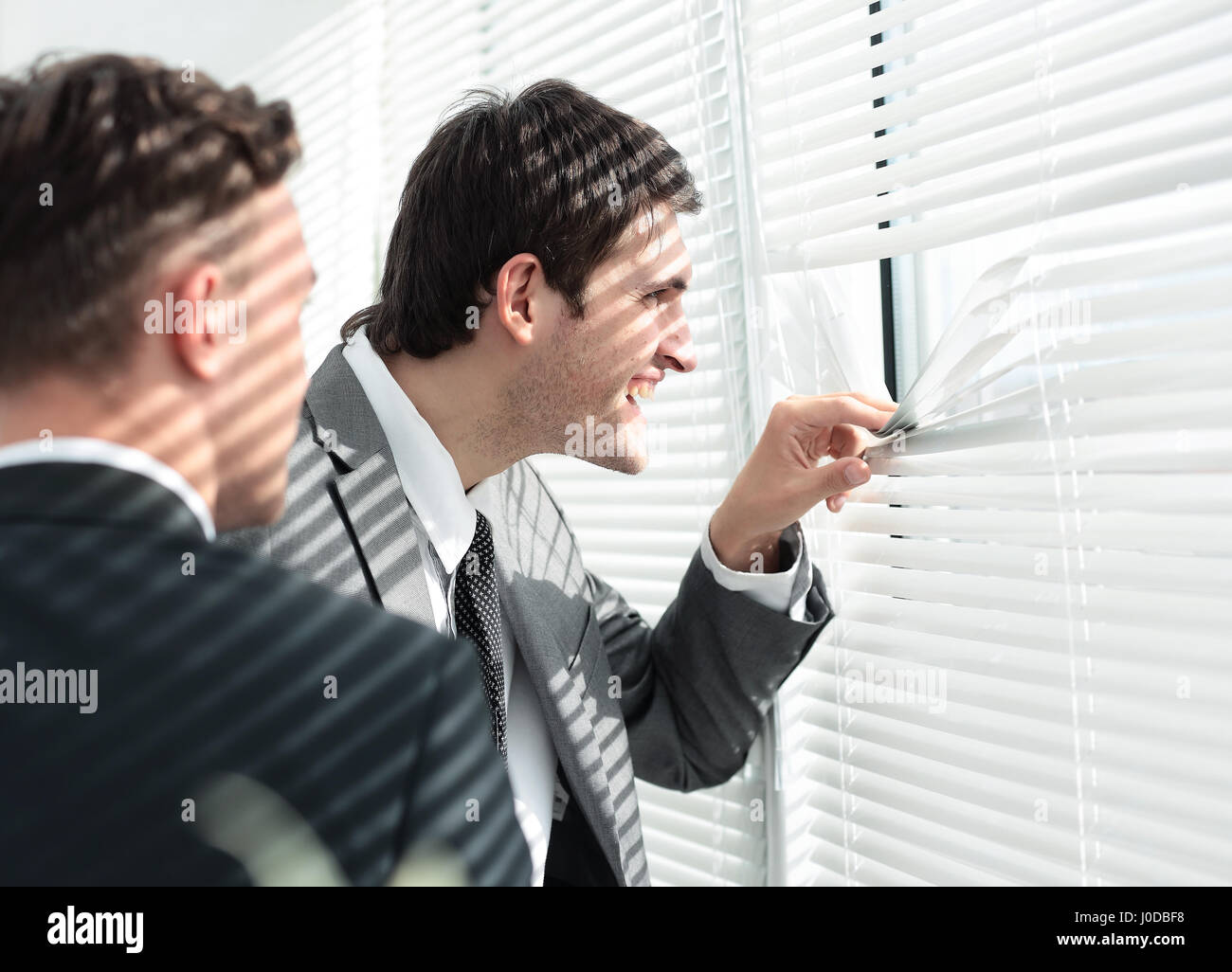 photo side view, smiling office staff pushes the curtain and looks out ...