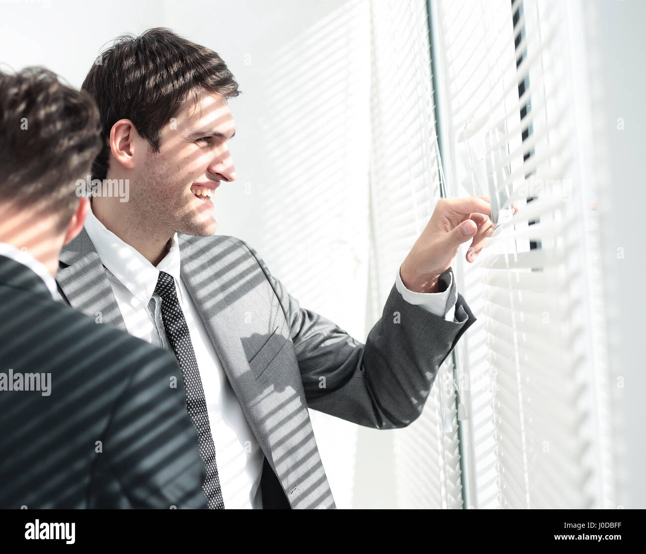 photo side view, smiling office staff pushes the curtain and looks out ...
