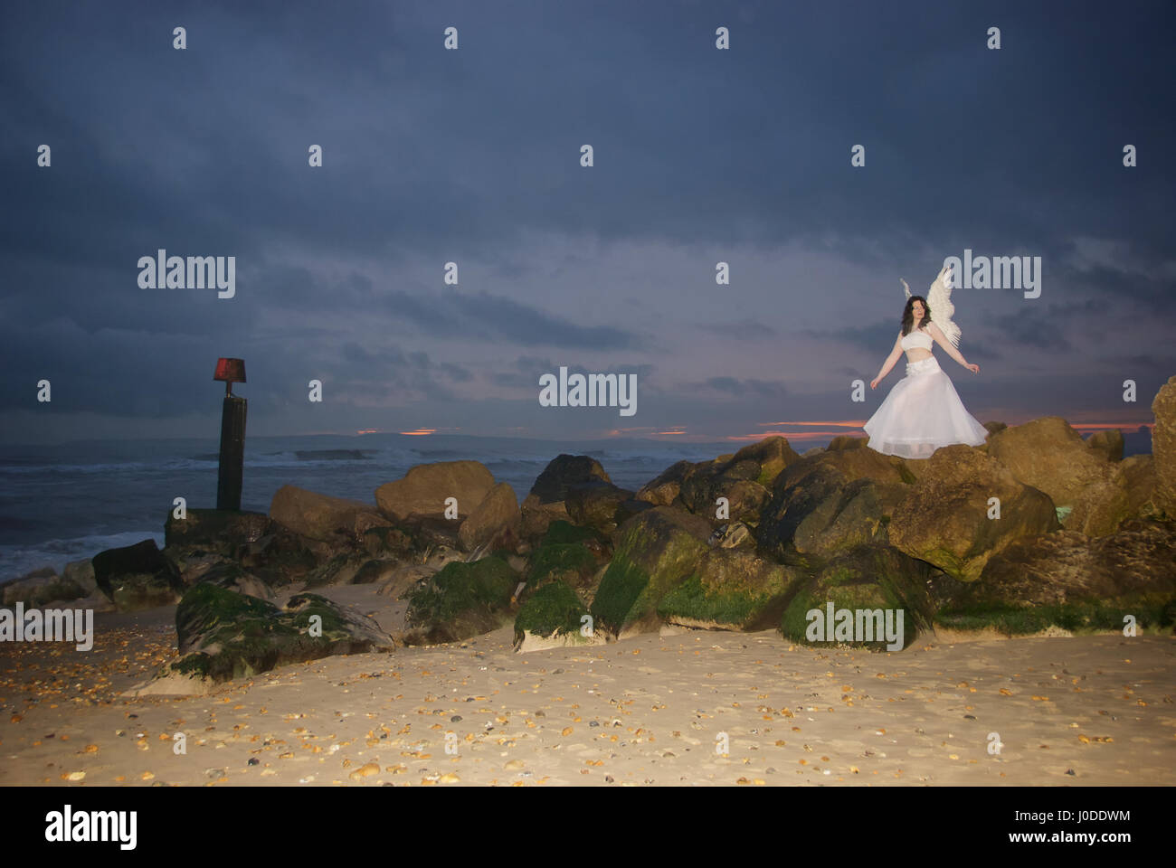Beautiful brunette girl dressed as an angel on the rocks at sunset ...