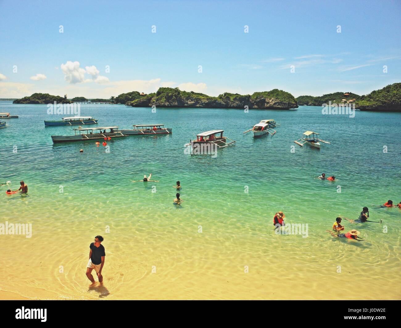 People swimming in a shallow beach with boats and islands in the ...