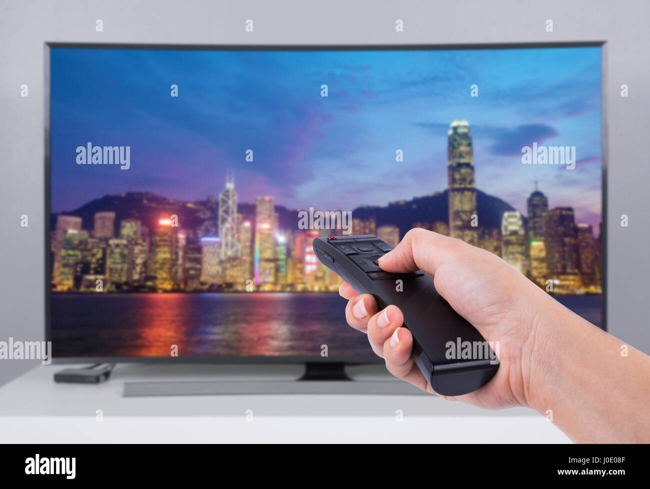 Hand holding TV remote control with a television and city screen in the ...