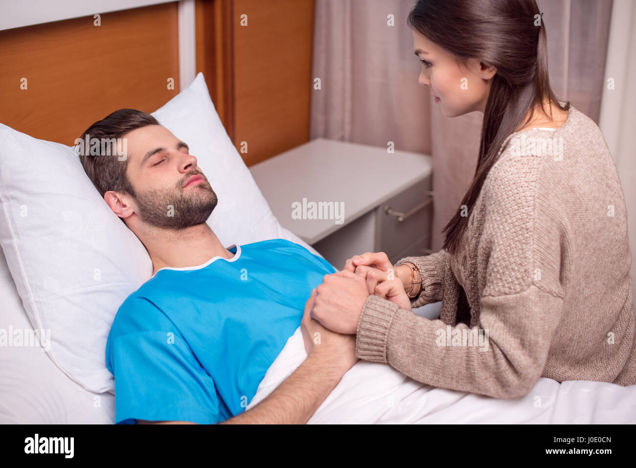 Young woman visiting sick man in hospital holding his hands Stock Photo ...