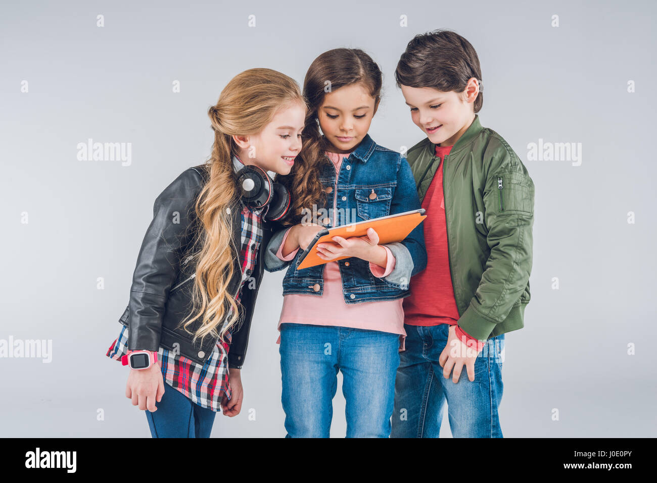 Three cute little kids using digital tablet together on grey Stock ...