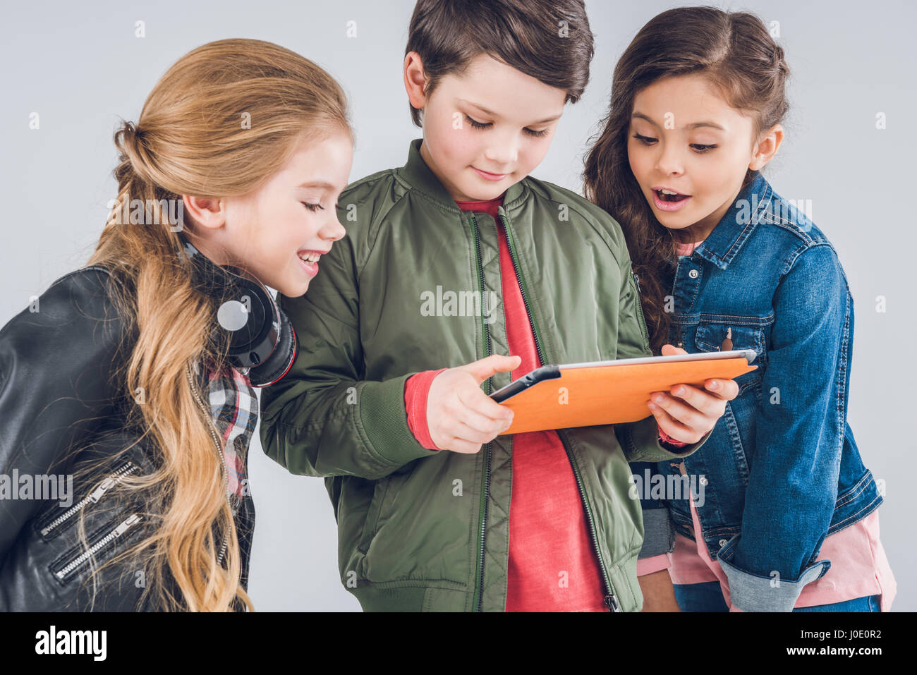 Three cute little kids using digital tablet together on grey Stock ...