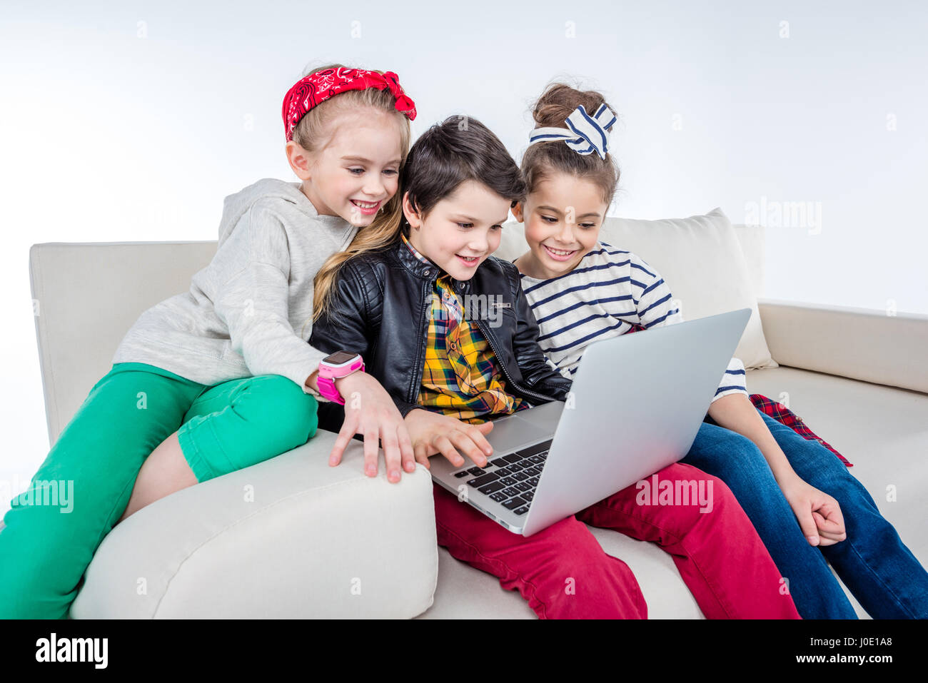 side view of smiling children using laptop while sitting on sofa Stock ...